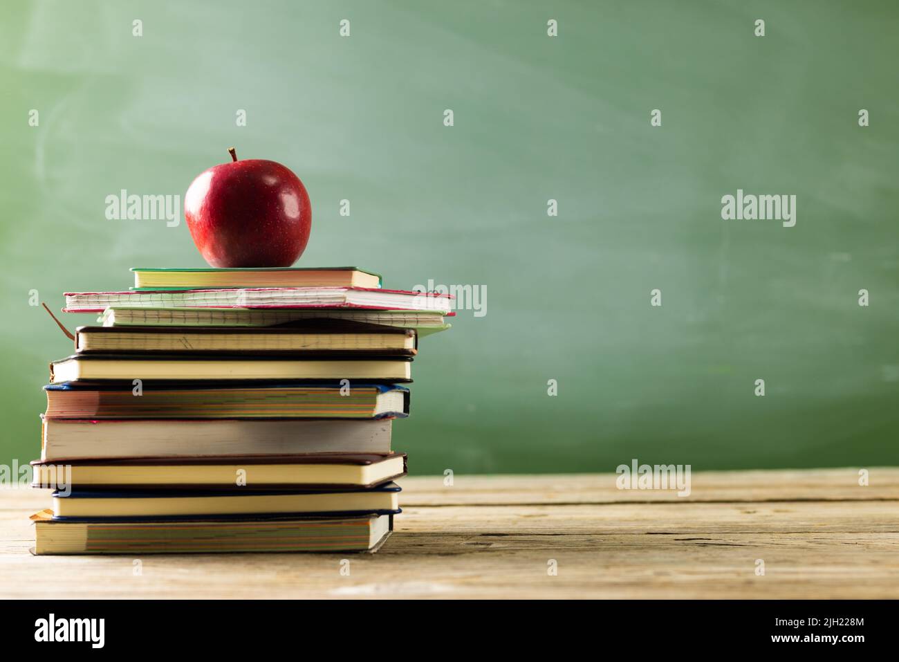 Image of books, notebook and apple on wooden table over black board ...