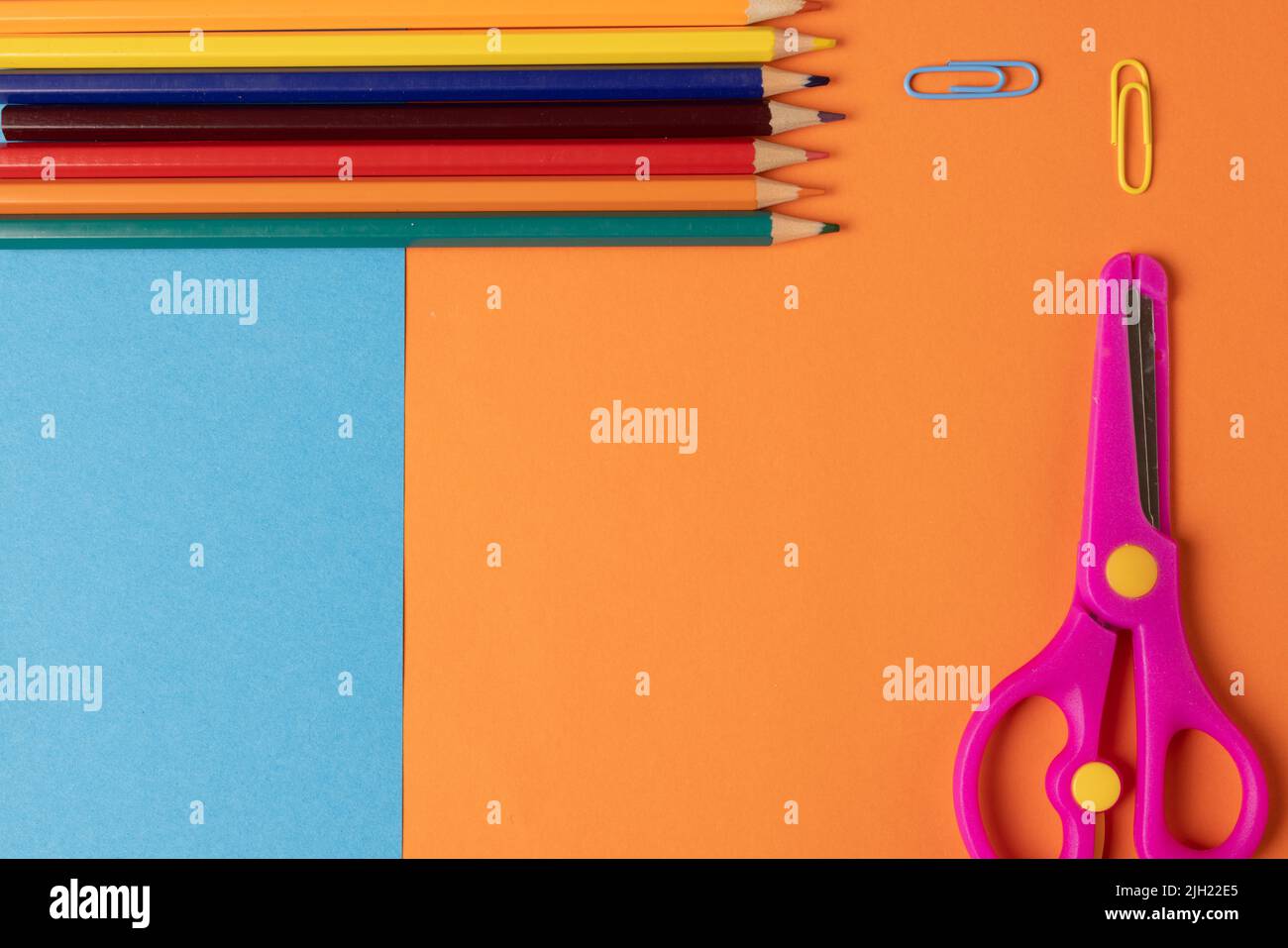 Composition of crayons, scissors and clips on blue and orange surface ...