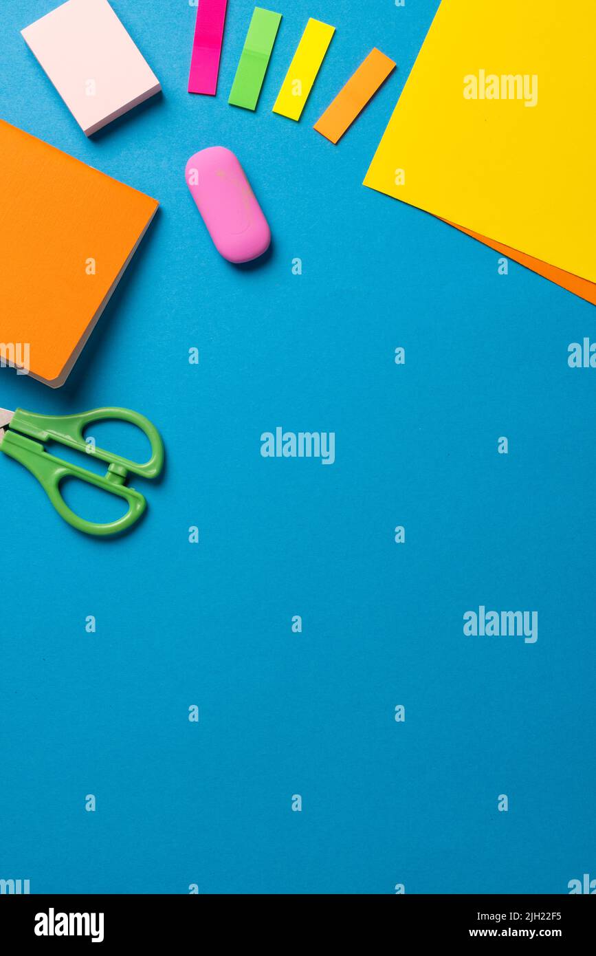 Vertical composition of post its, eraser, crayons and scissors on blue ...