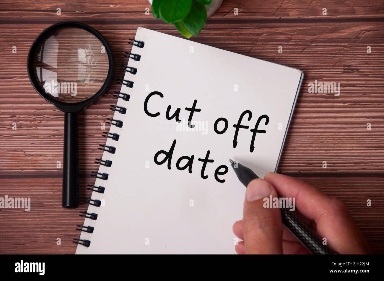 Hand writing cut of date on notepad with table plant and magnifying ...