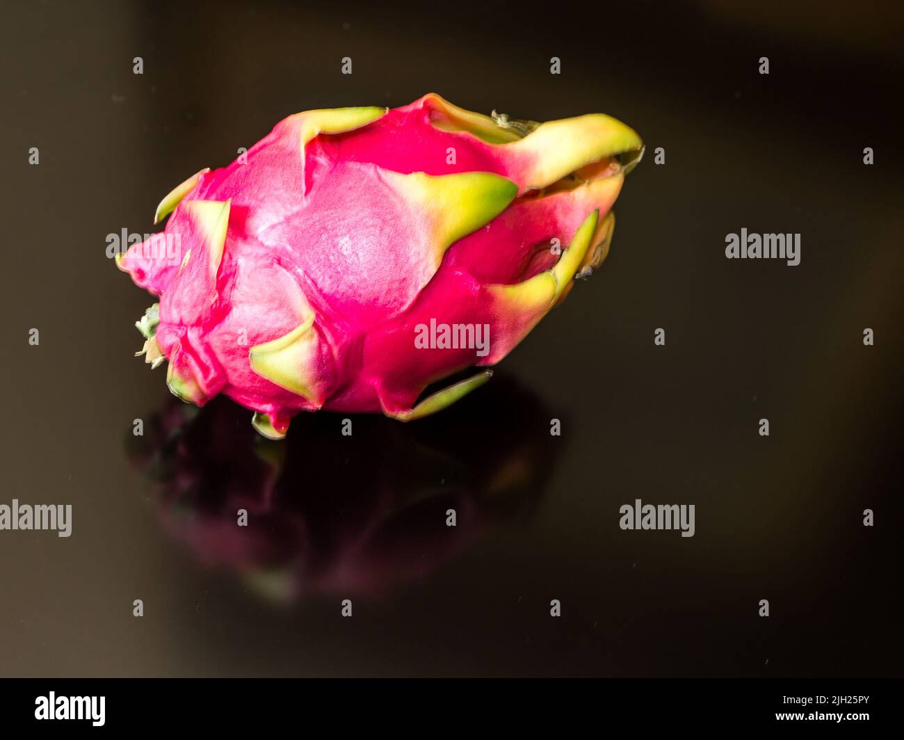 A single small pink Dragon fruit on a shiny black surface Stock Photo ...