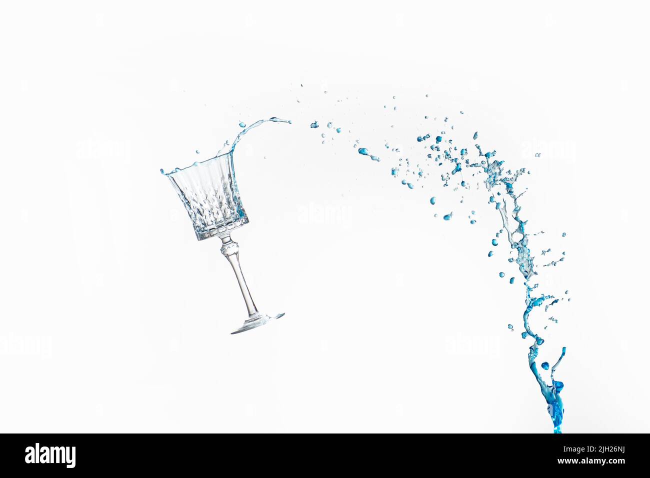 Blue liquid spillig from a pattered square beverage glass. Over white ...