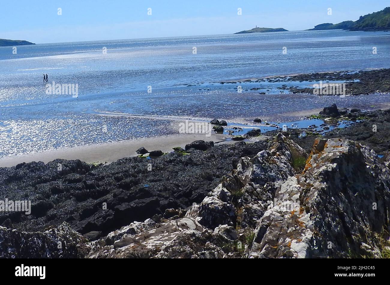 A pair of lone walkers cross the beach at Dhoon Bay, Kirkcudbright ...