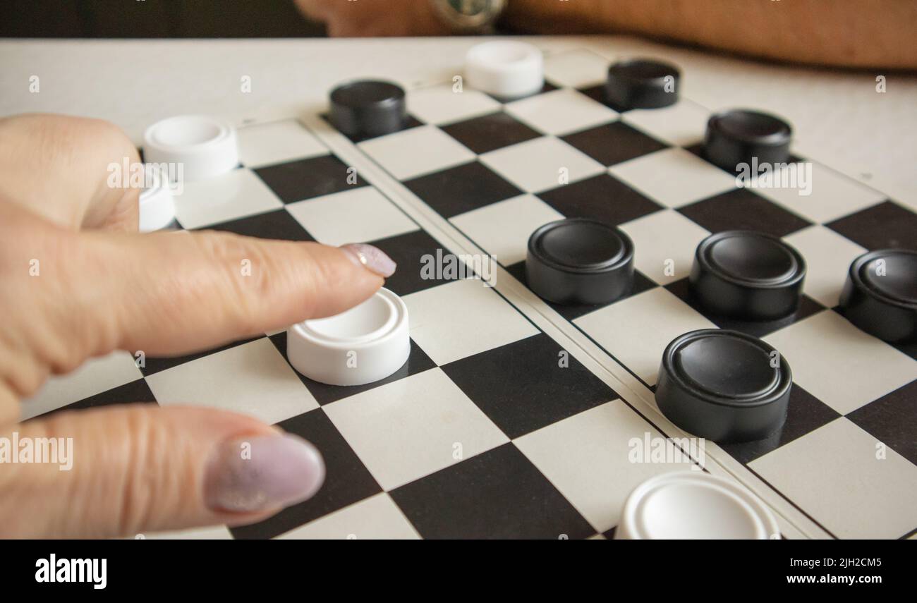 A woman's hand moves a white checker on a black-and-white playing field ...