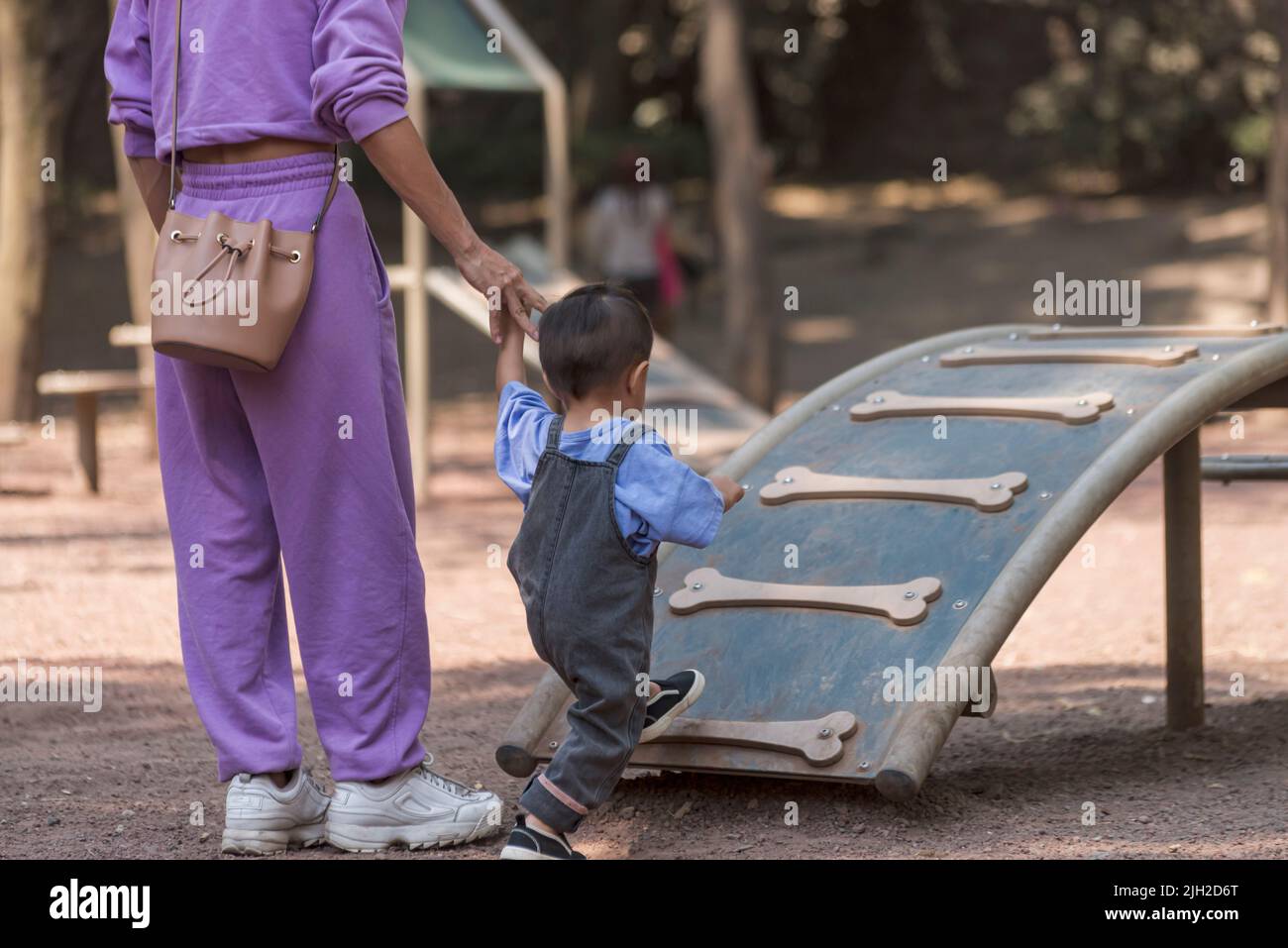 Baby boy playing at the park climbing a ramp holding his mom's hand ...