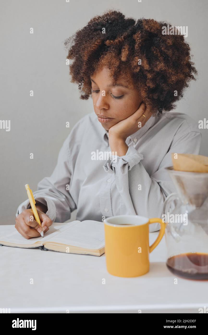 A curly African American woman makes notes in her diary at breakfast ...