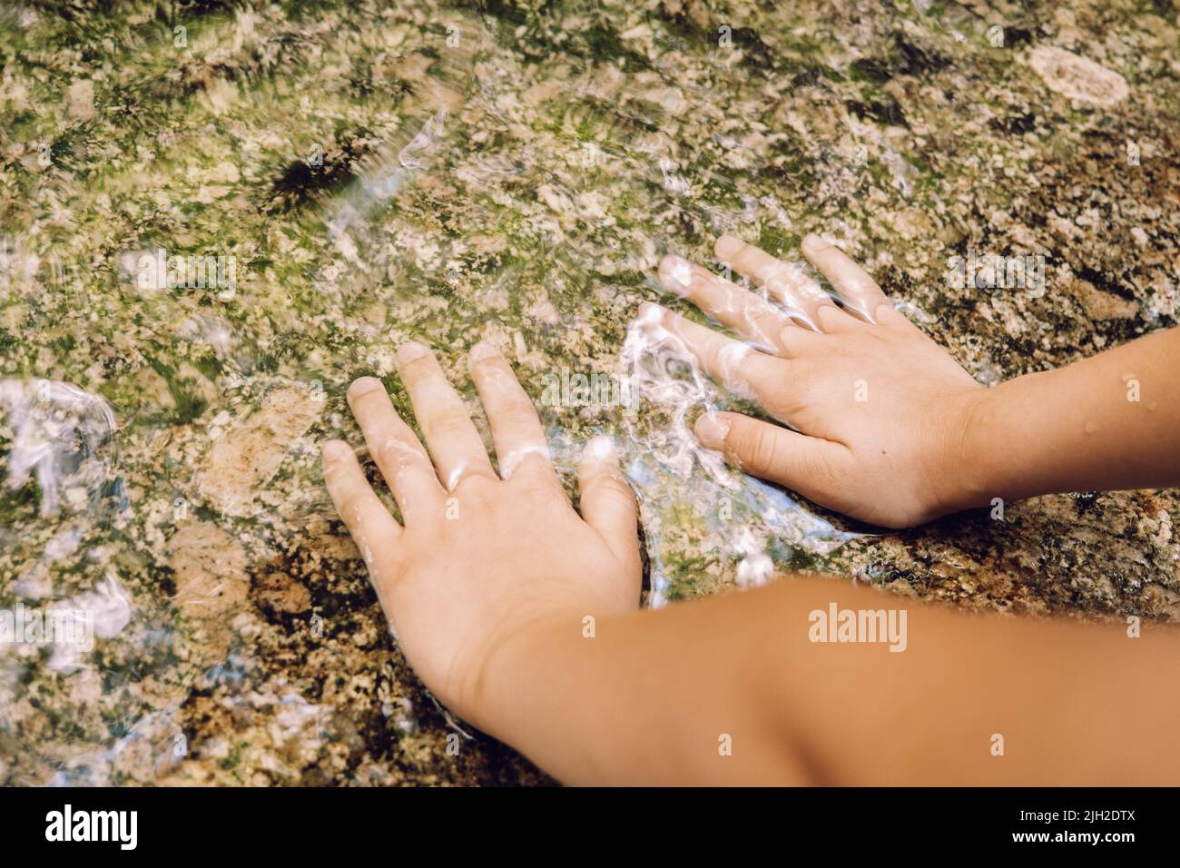 Kid touches cold water in waterfall Stock Photo - Alamy