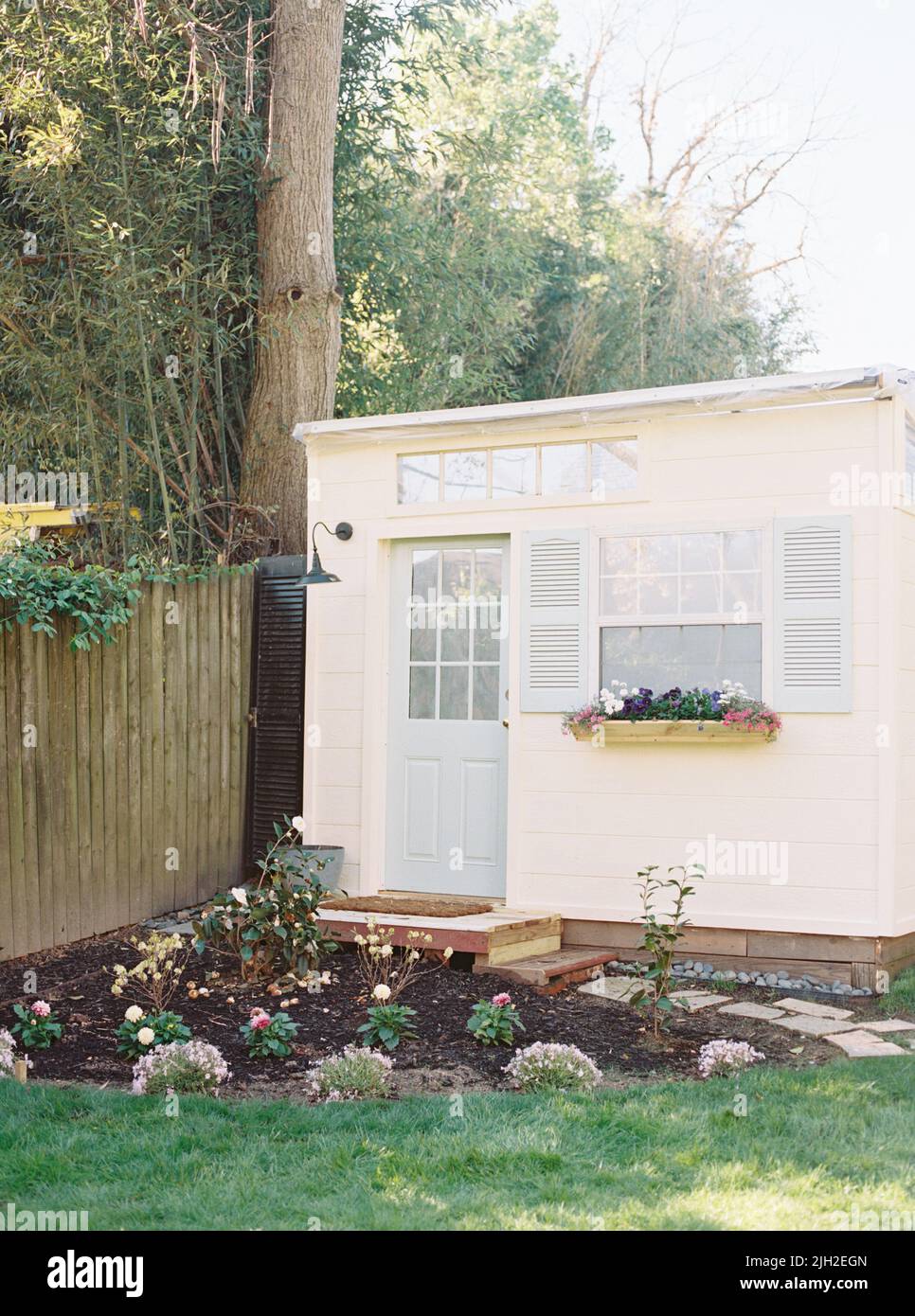 Small ivory shed with blue shutters and garden Stock Photo - Alamy