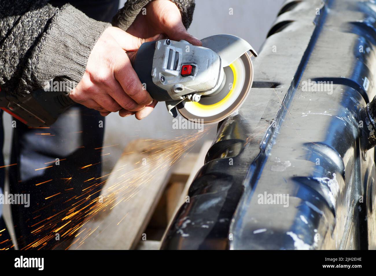 A man grinds a metal tank with a grinder Stock Photo - Alamy