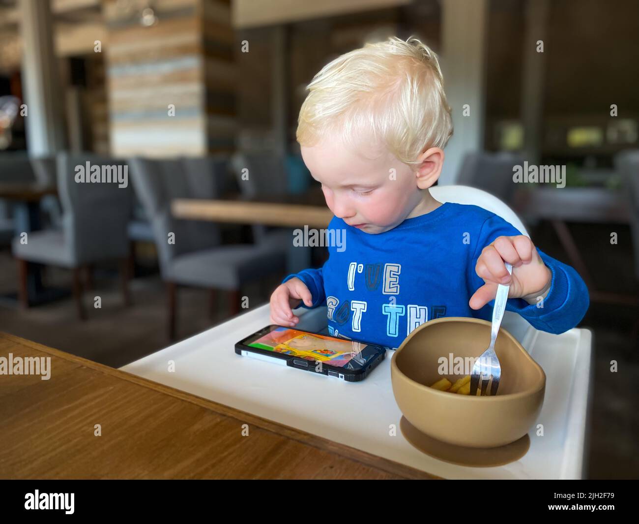 Toddler is eating and looking at the phone Stock Photo - Alamy