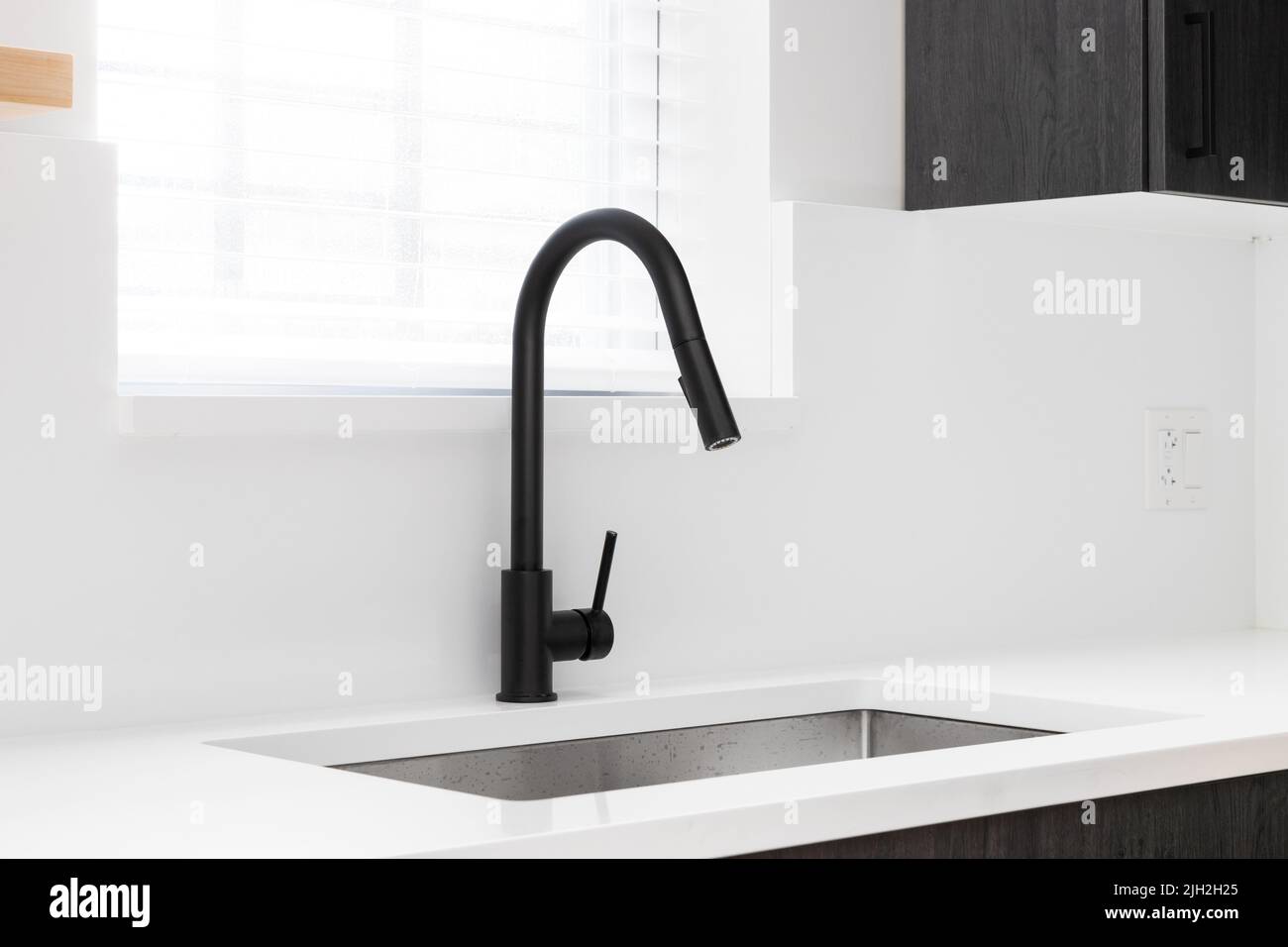 A kitchen sink detail shot with dark wooden cabinets, a black faucet ...