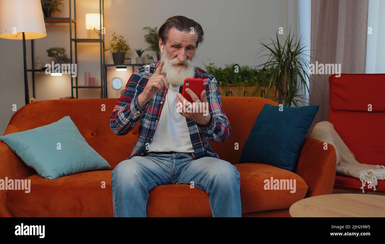 Senior old grandfather man wearing earphones making phone online ...