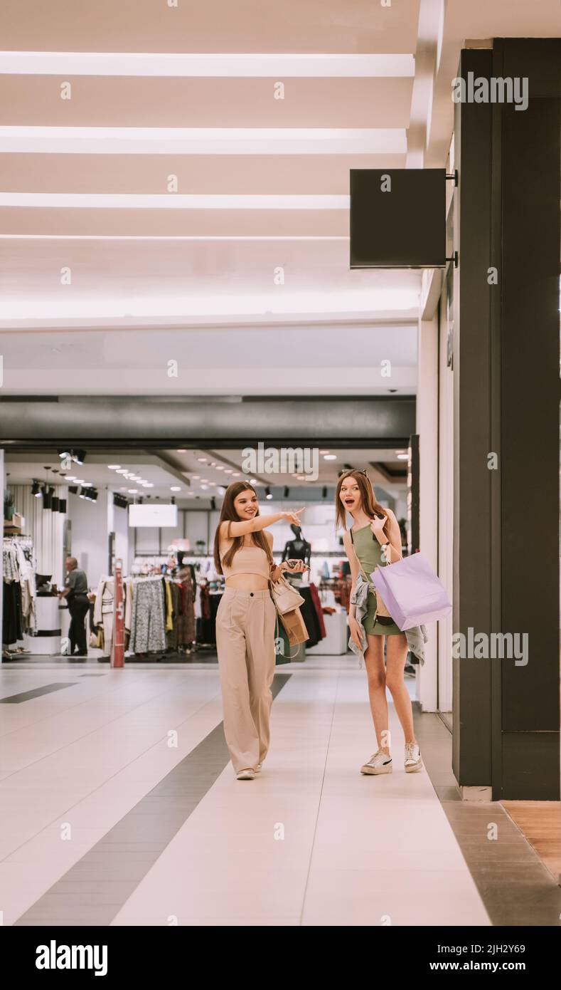 Two pretty best friends walking at the mall while one of the pointing ...