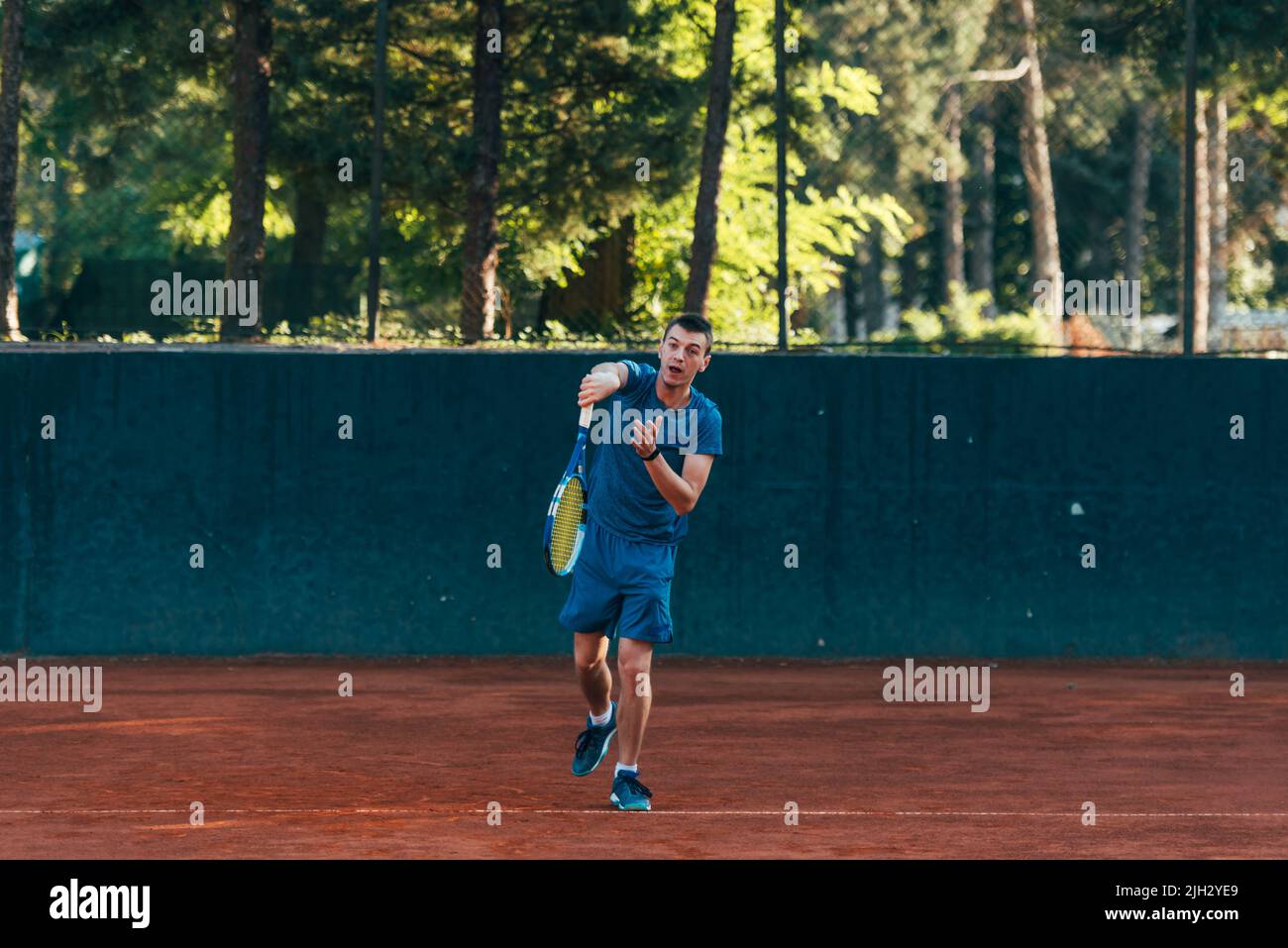 A professional tennis player is serving ball on a clay tennis court ...