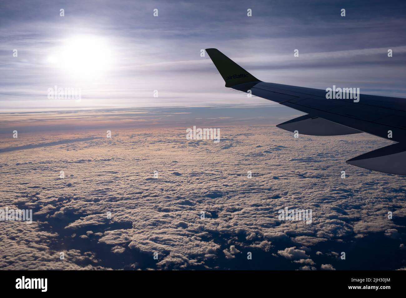 Airbus A220-300 wings in sunset lights flying above clouds somewhere ...