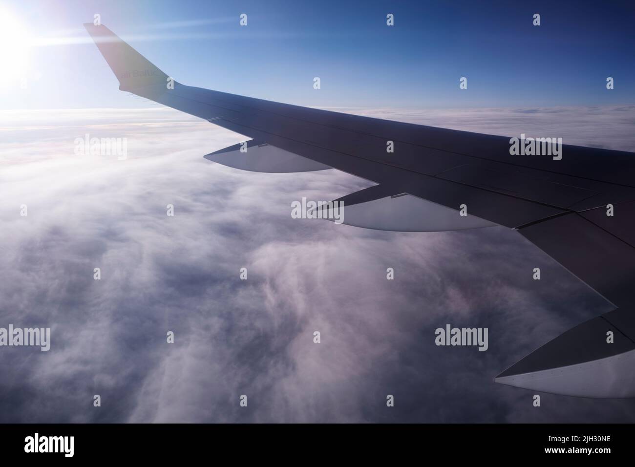 Airbus A220-300 wings in sunset lights flying above clouds somewhere ...