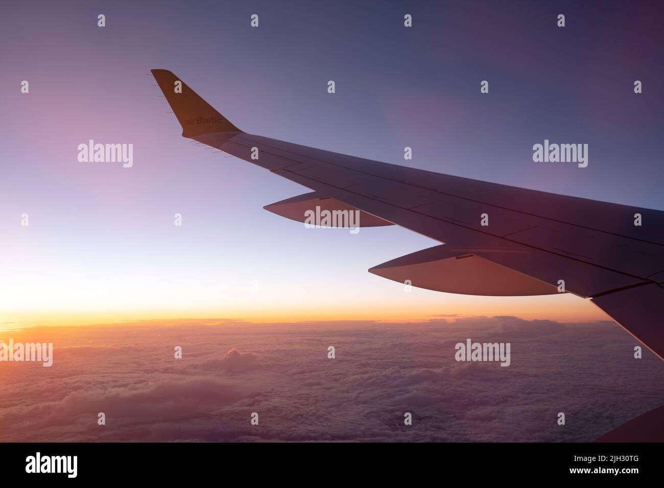Airbus A220-300 wings in sunset lights flying above clouds somewhere ...