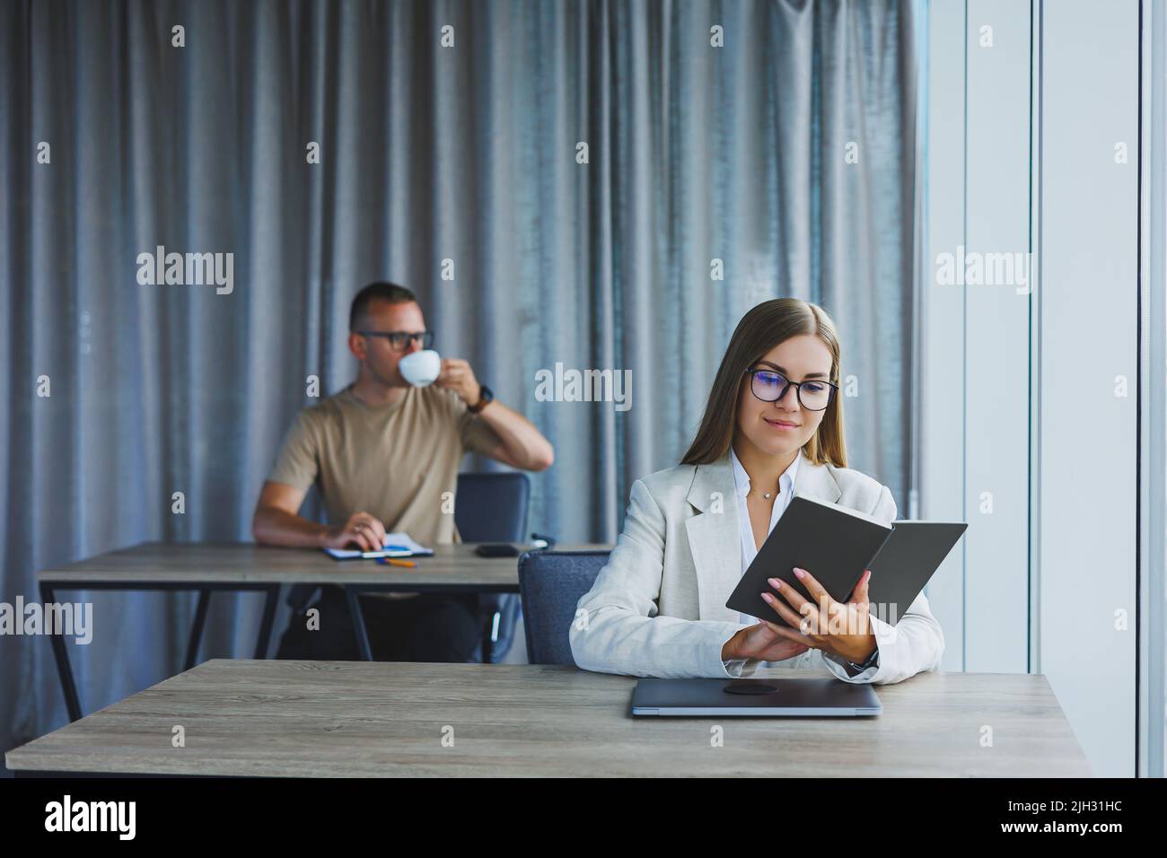 A business woman is holding a notepad and using a laptop while her ...