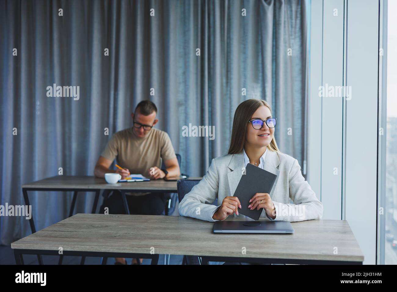 A business woman is holding a notepad and using a laptop while her ...