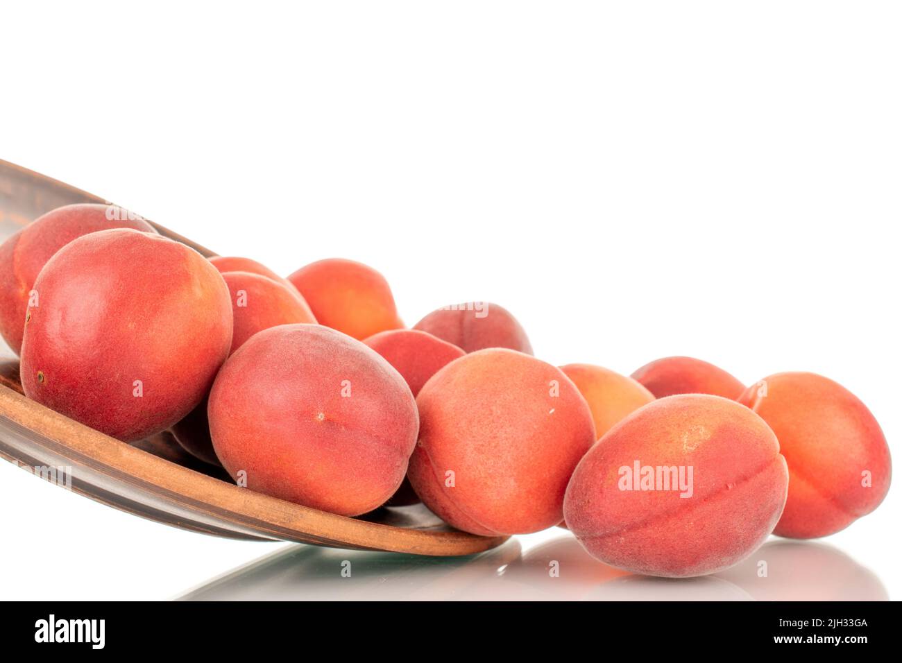 Several ripe red apricots on a clay dish, close-up, isolated on a white ...