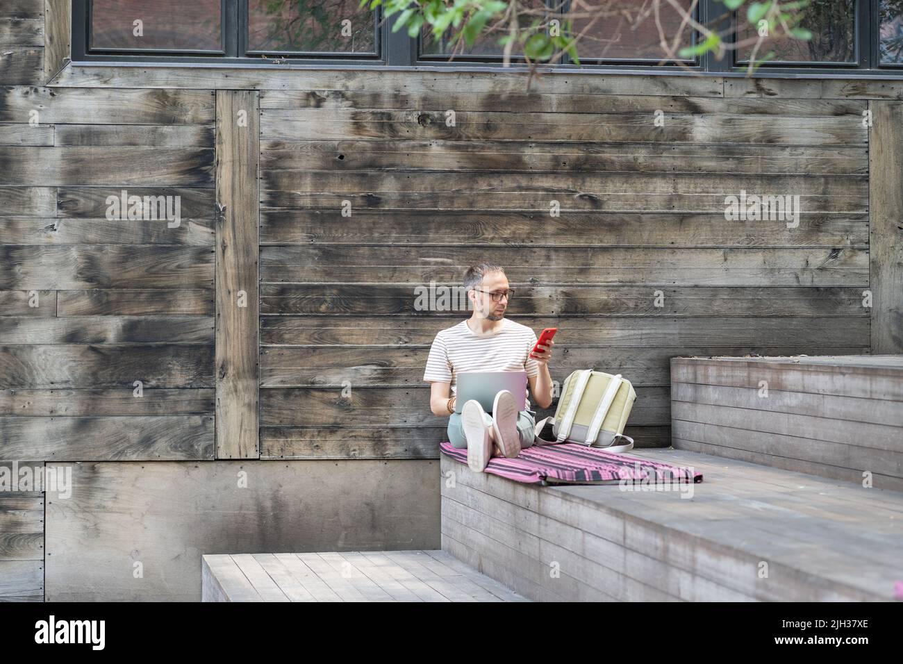 Software developer wearing glasses using laptop and phone, distracted ...