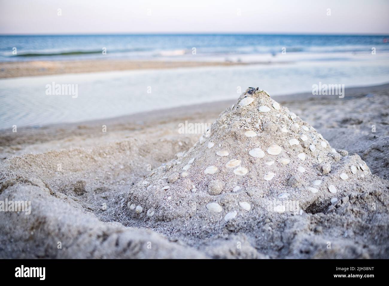 A sand castle stands on the beach near sea water under the bright sun ...