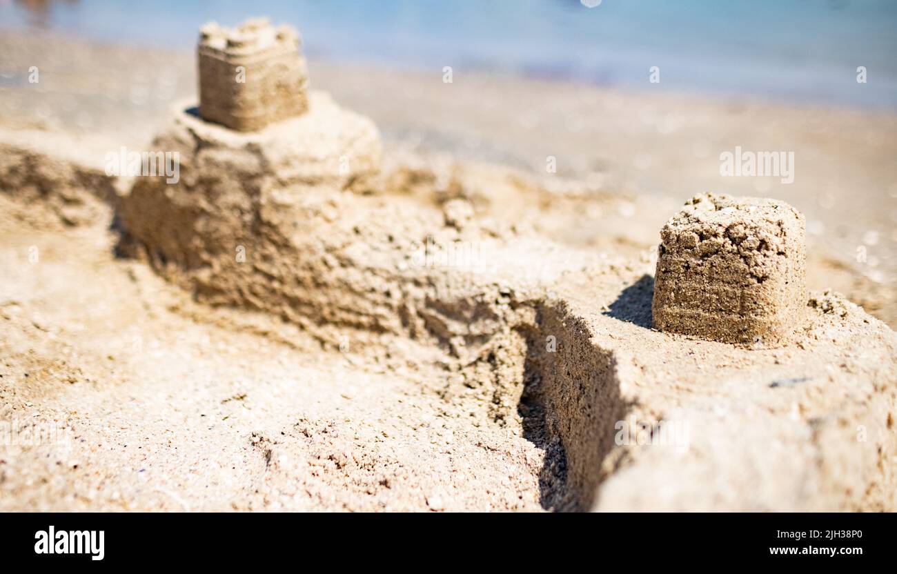 A sand castle stands on the beach near sea water under the bright sun ...