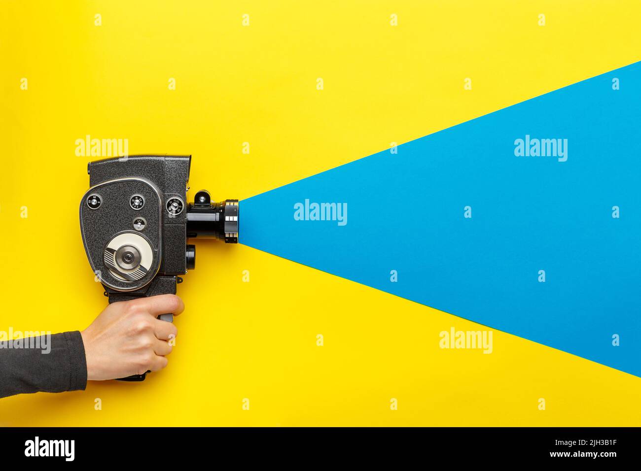 Female hand holding old style film movie camera on a yellow background ...