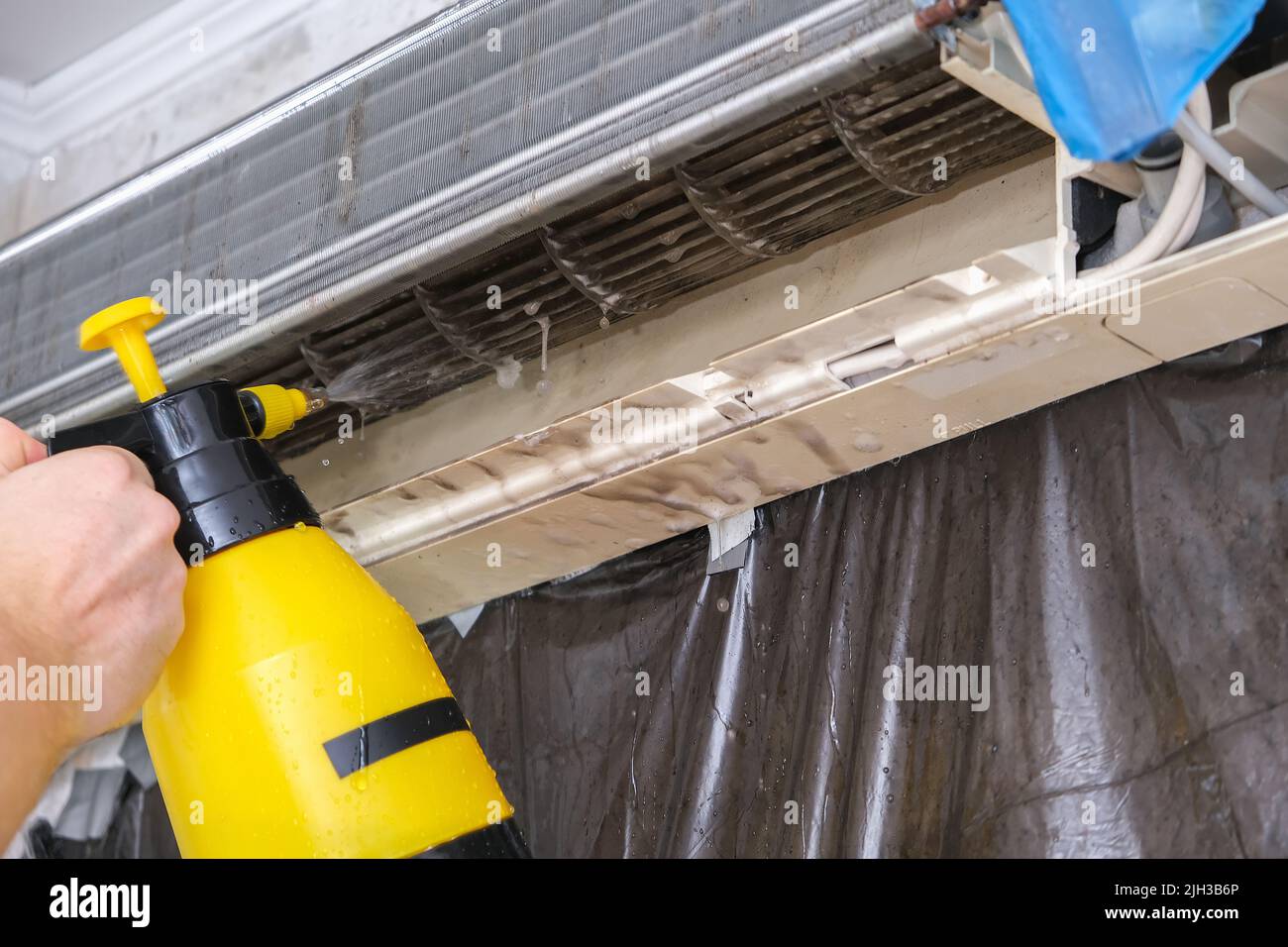 A man washes off a special foam for cleaning air conditioners with a ...