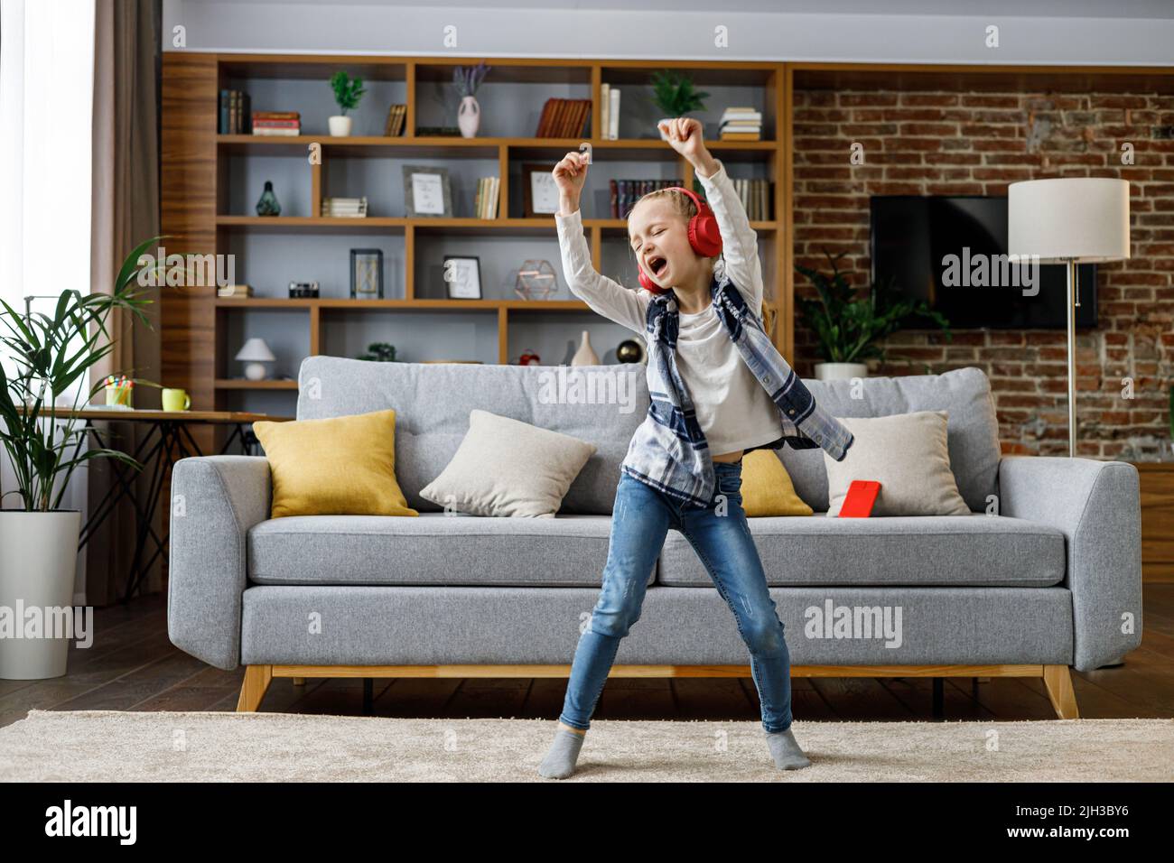 Happy little girl wearing red headphones dancing and singing, jumping ...