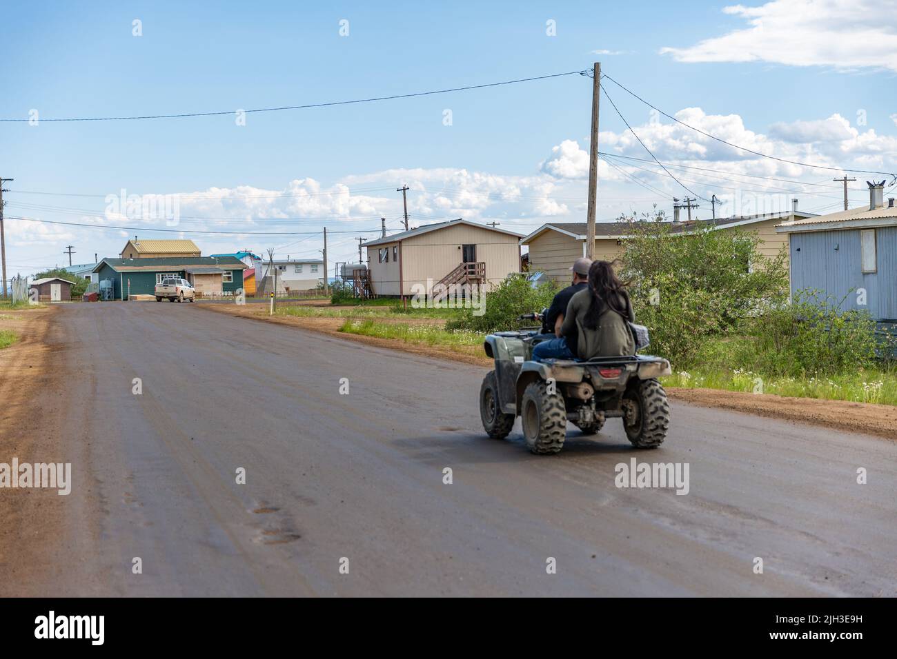 Two people riding a four-wheeler in summer on the dirt road of the ...