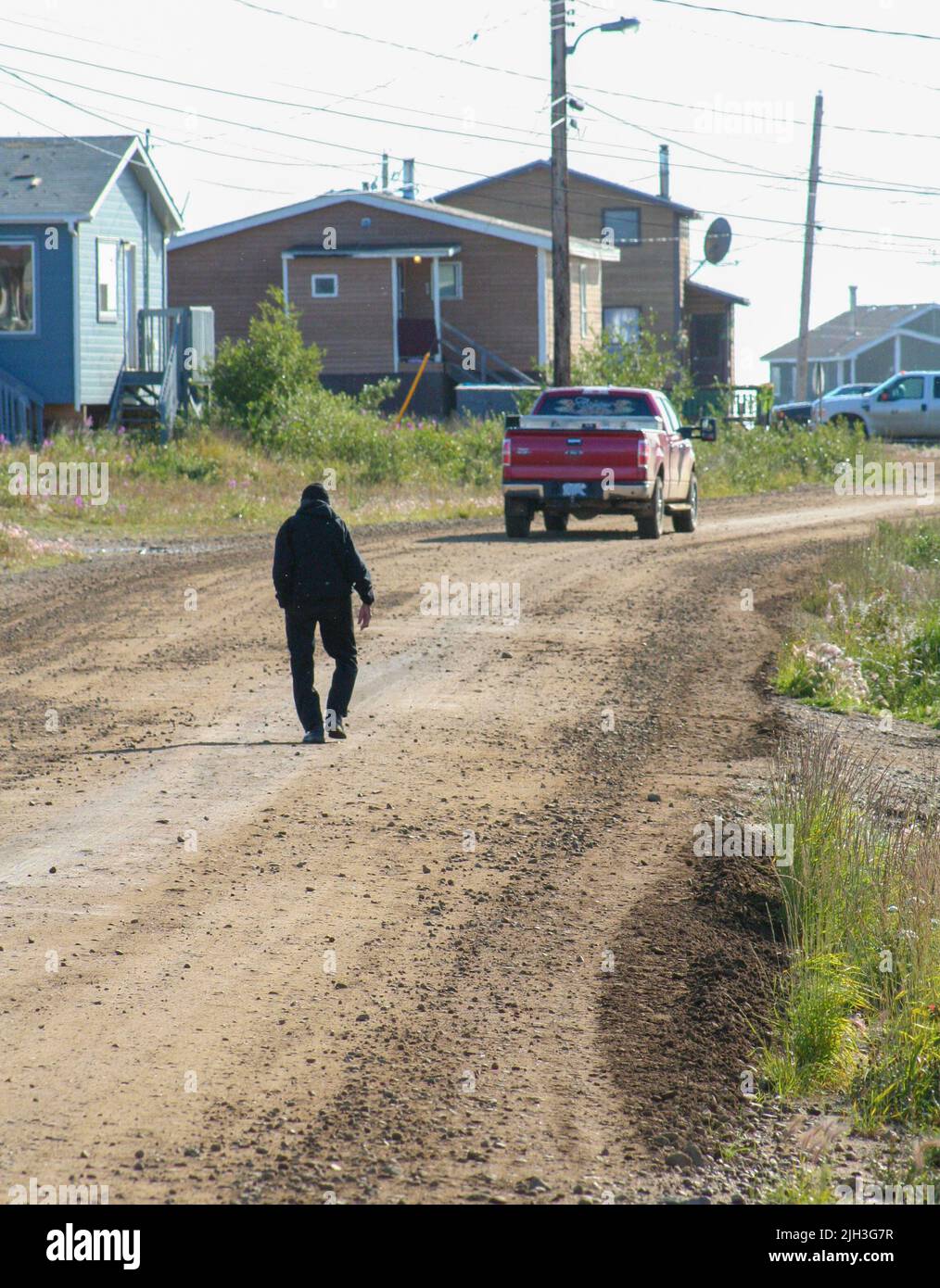 An elderly man walking along dirt road of Indigenous northern community ...