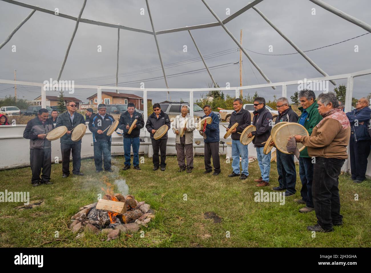 Indigenous Dene men with traditional drums performing fire feeding ...
