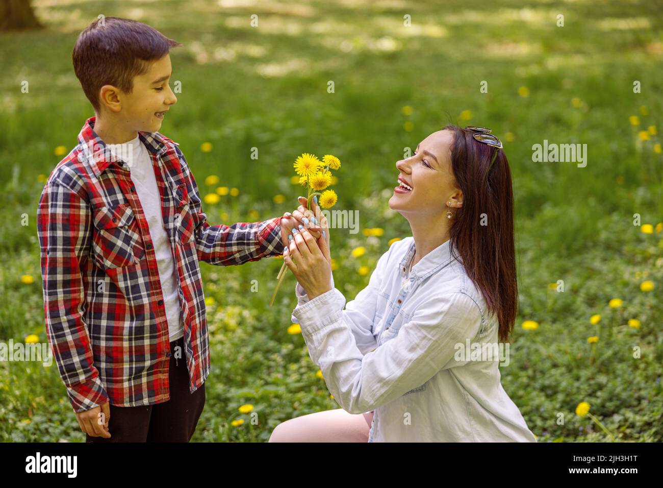 Cute son handing flowers to pretty mother. Little boy giving dandelions ...