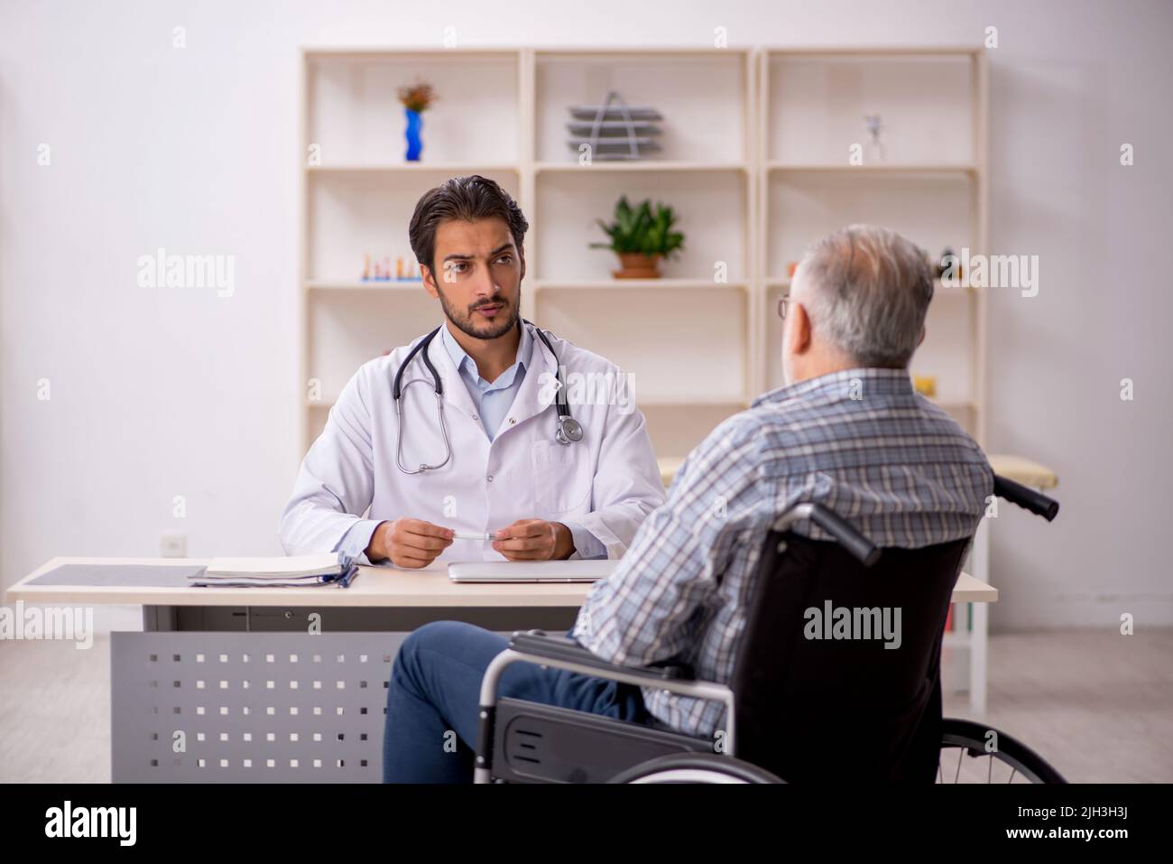 Old male patient in wheelchair visiting young male doctor Stock Photo ...