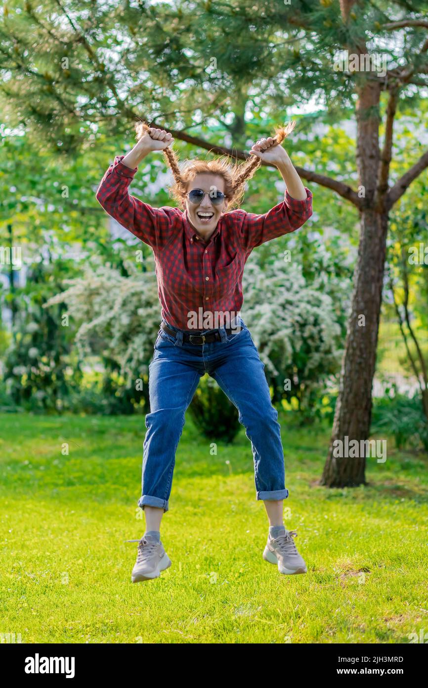 A laughing woman hangs in the air holding herself by two braids in ...