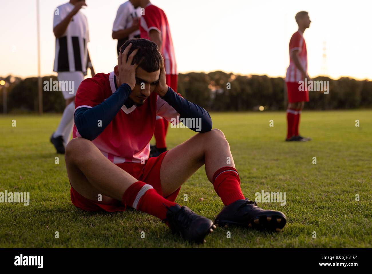 Caucasian sad athlete with head in hands sitting on land with players ...