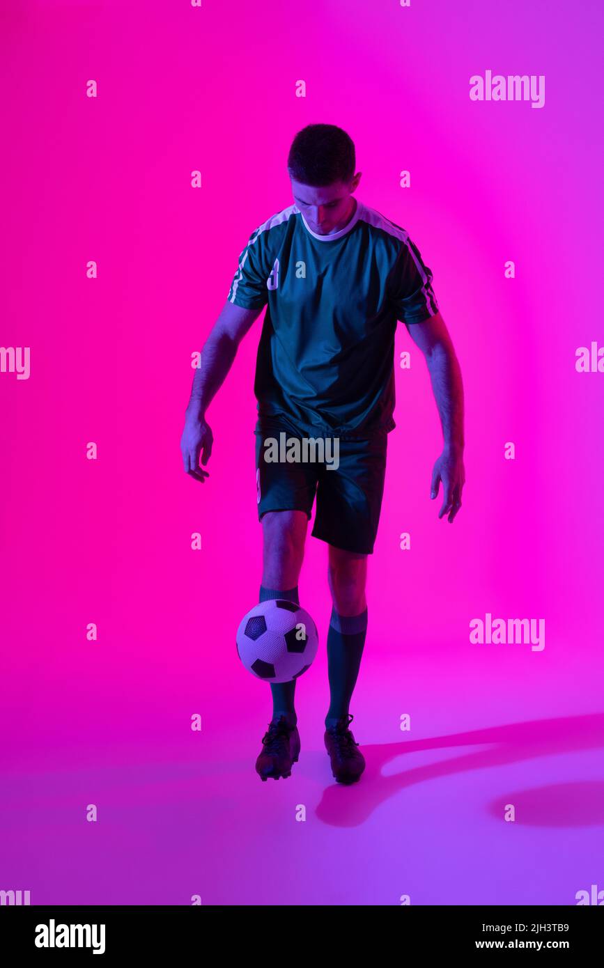 Caucasian male soccer player kicking football over neon pink lighting ...