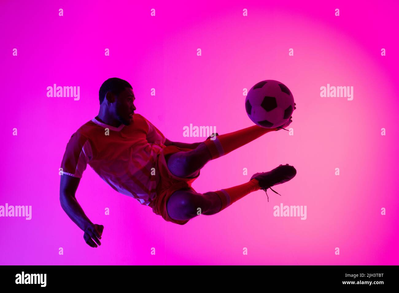 African american male soccer player kicking football over neon pink ...