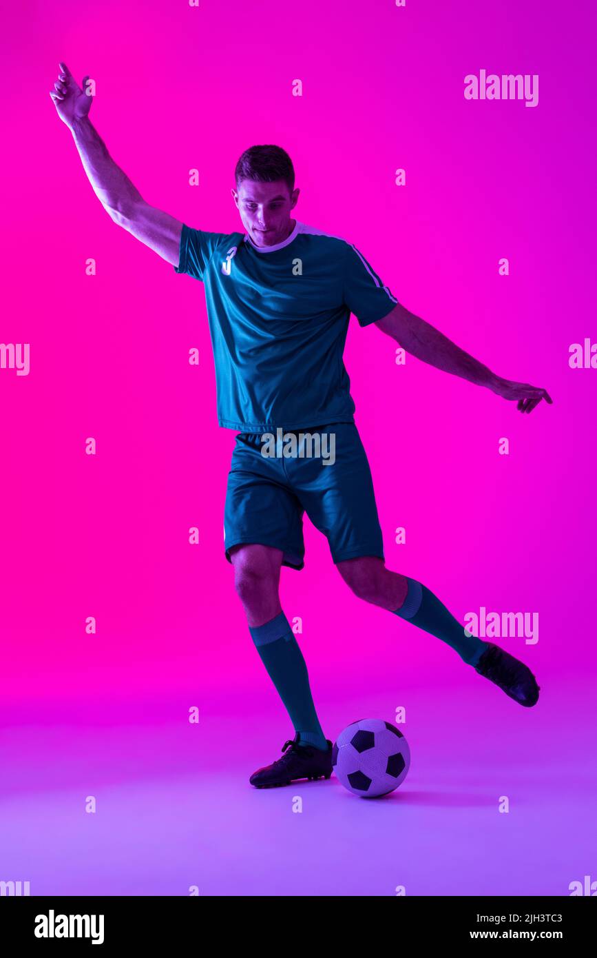 Caucasian male soccer player kicking football over neon pink lighting ...