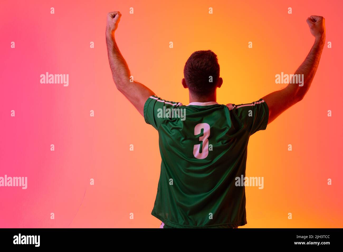 Caucasian male soccer player raising hands over neon pink lighting ...