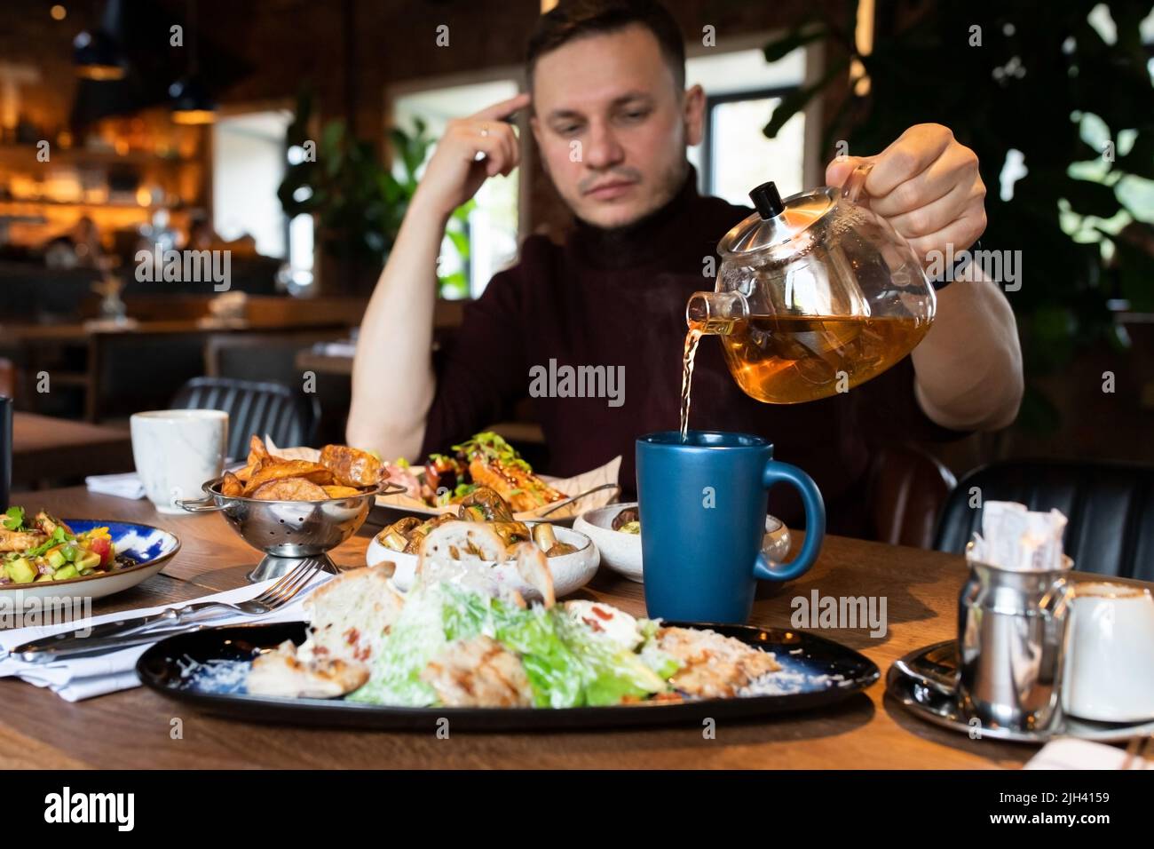 A man in a restaurant pours himself a mug of hot tea from a glass ...