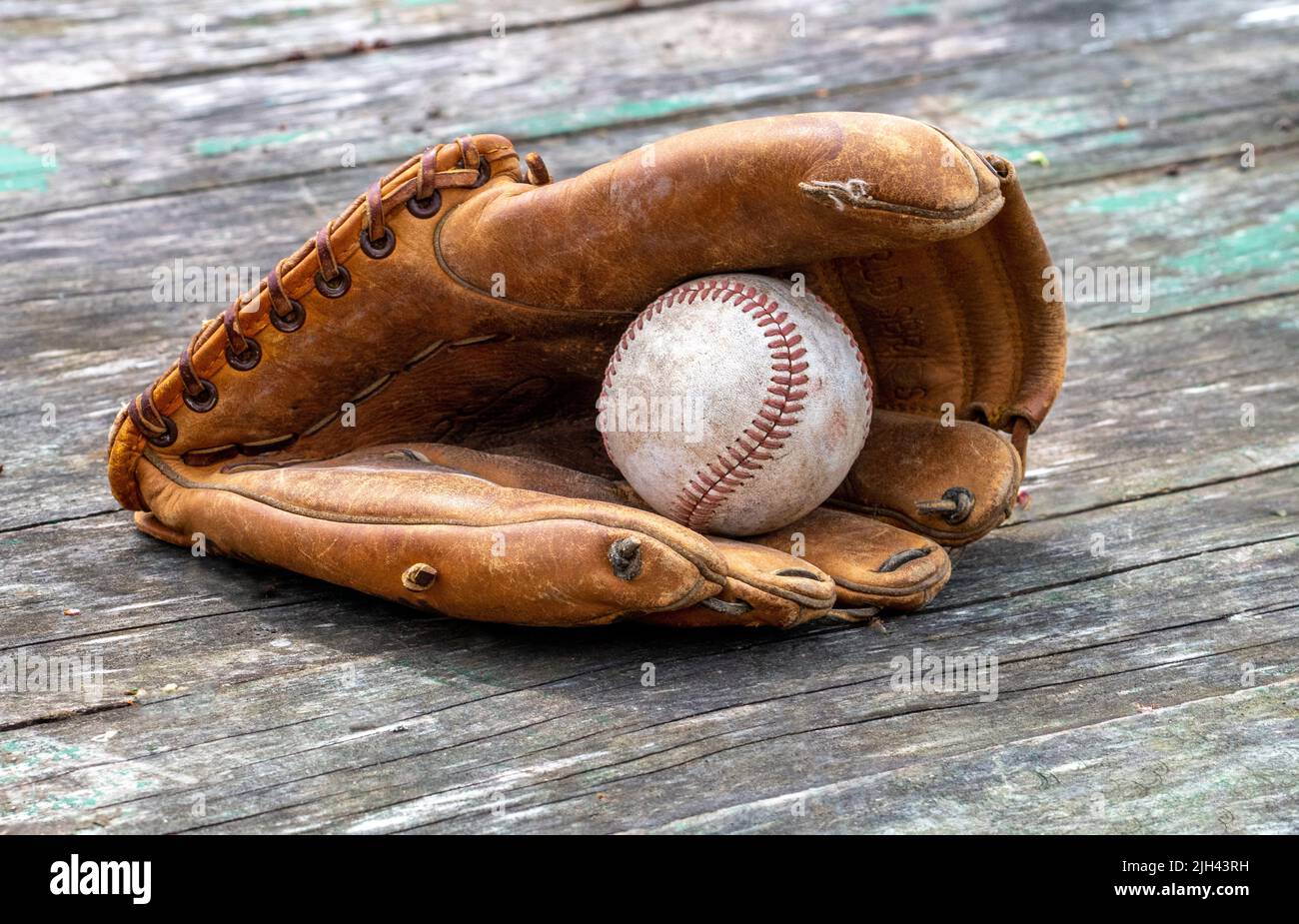 Old worn baseball glove holds an ancient, dirty baseball, a beautiful ...