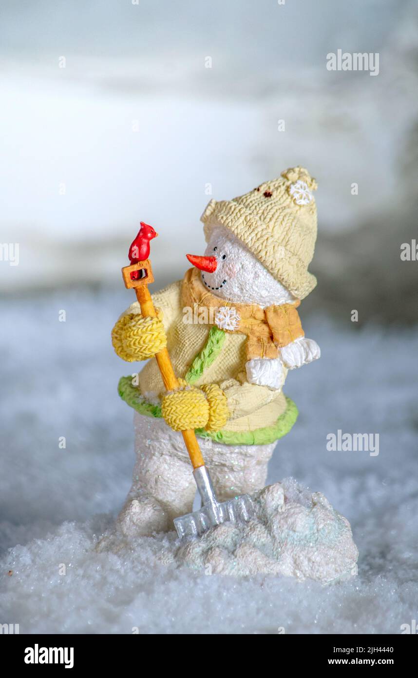 Comical snowman with a snow shovel, engages with a tiny red cardinal ...