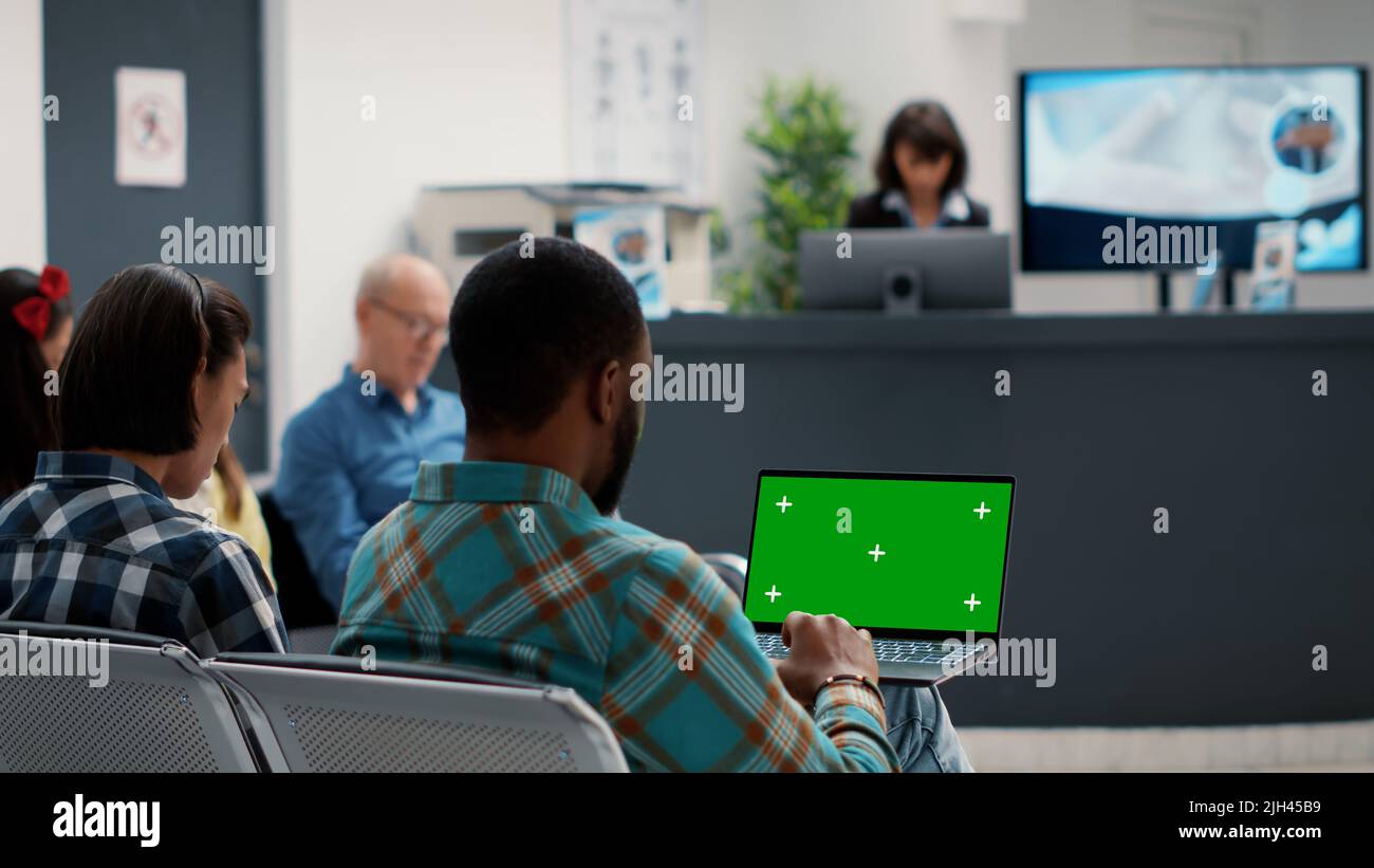 Young man holding greenscreen on laptop in hospital waiting room ...