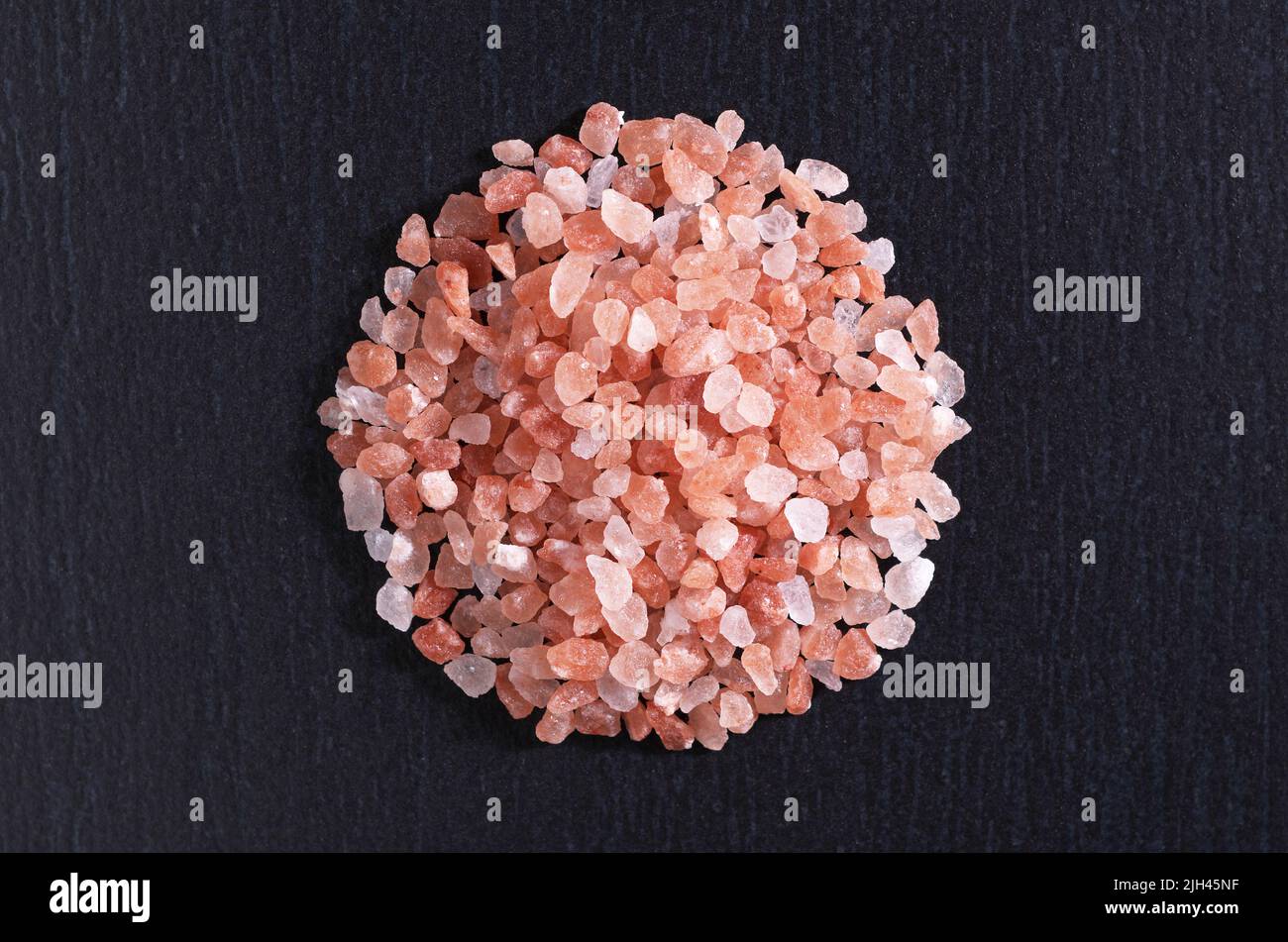 Pure, hand-mined Pink Salt, Coarse Grind on black stone background. Top ...