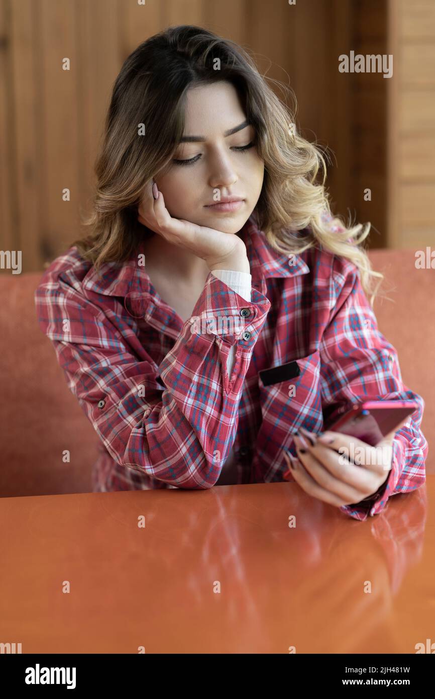 Thoughtful young girl looking out of window holding smartphone in hand ...