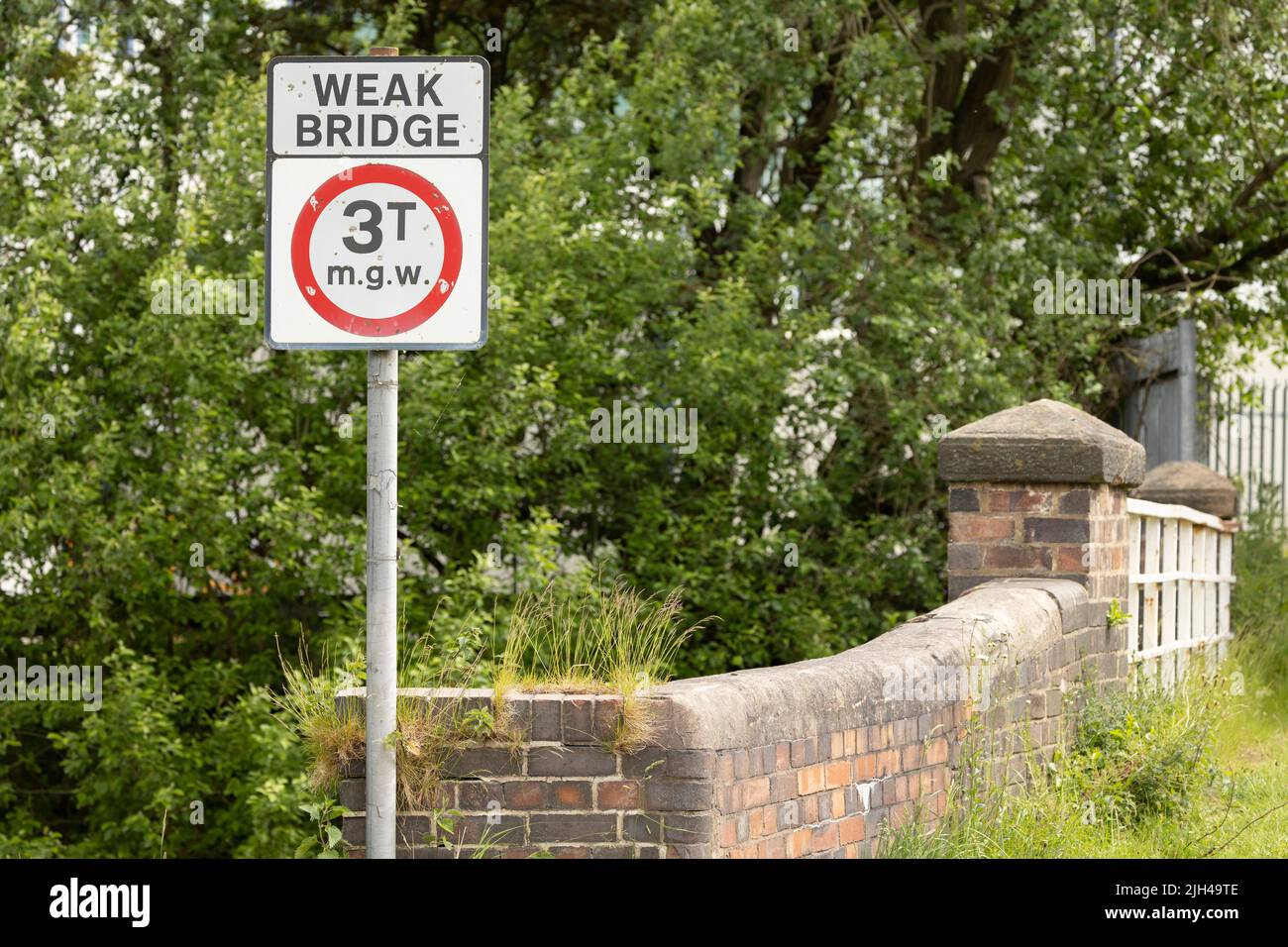 Outdoor white sign on a black pole showing a weak bridge with symbols ...