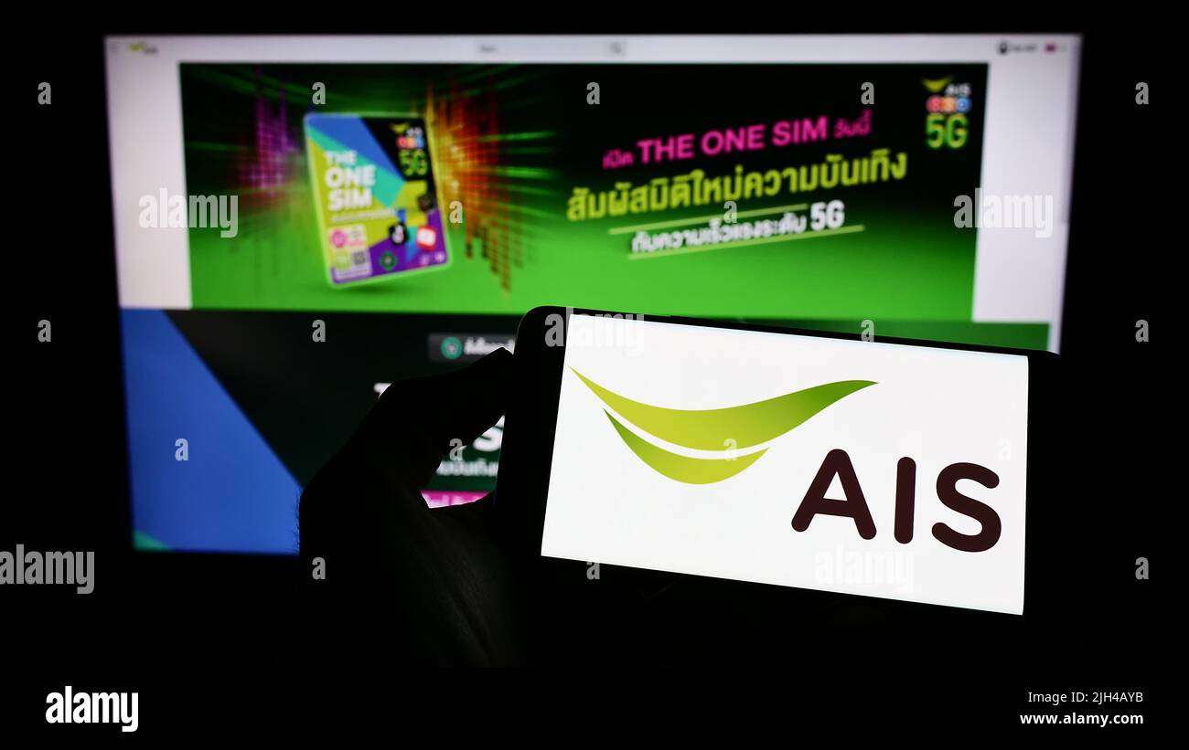 Person holding mobile phone with logo of Thai company Advanced Info Service (AIS) on screen in ...