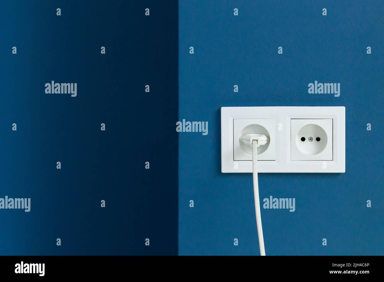 White electrical plug in the electric double socket on a blue wall ...